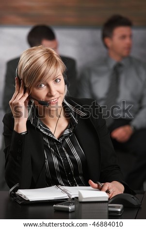 Young Receptionist Sitting At Desk In Office Recepcion, Talking On