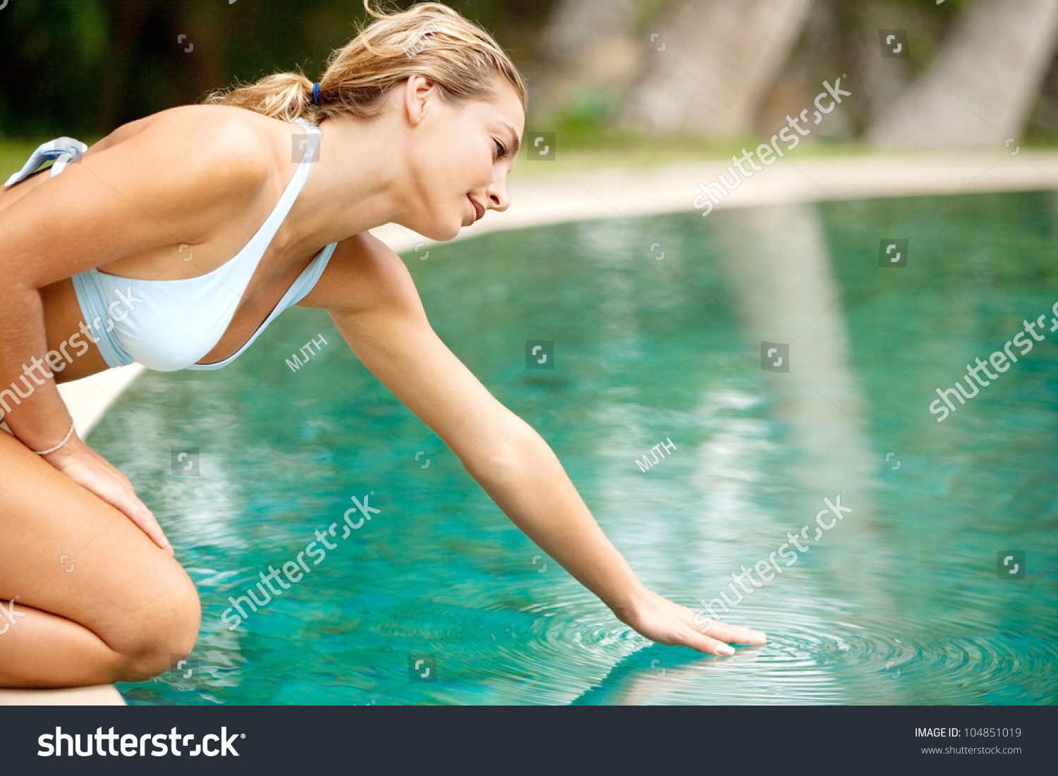 Attractive Young Woman Kneeling By The Edge Of A Swimming Pool