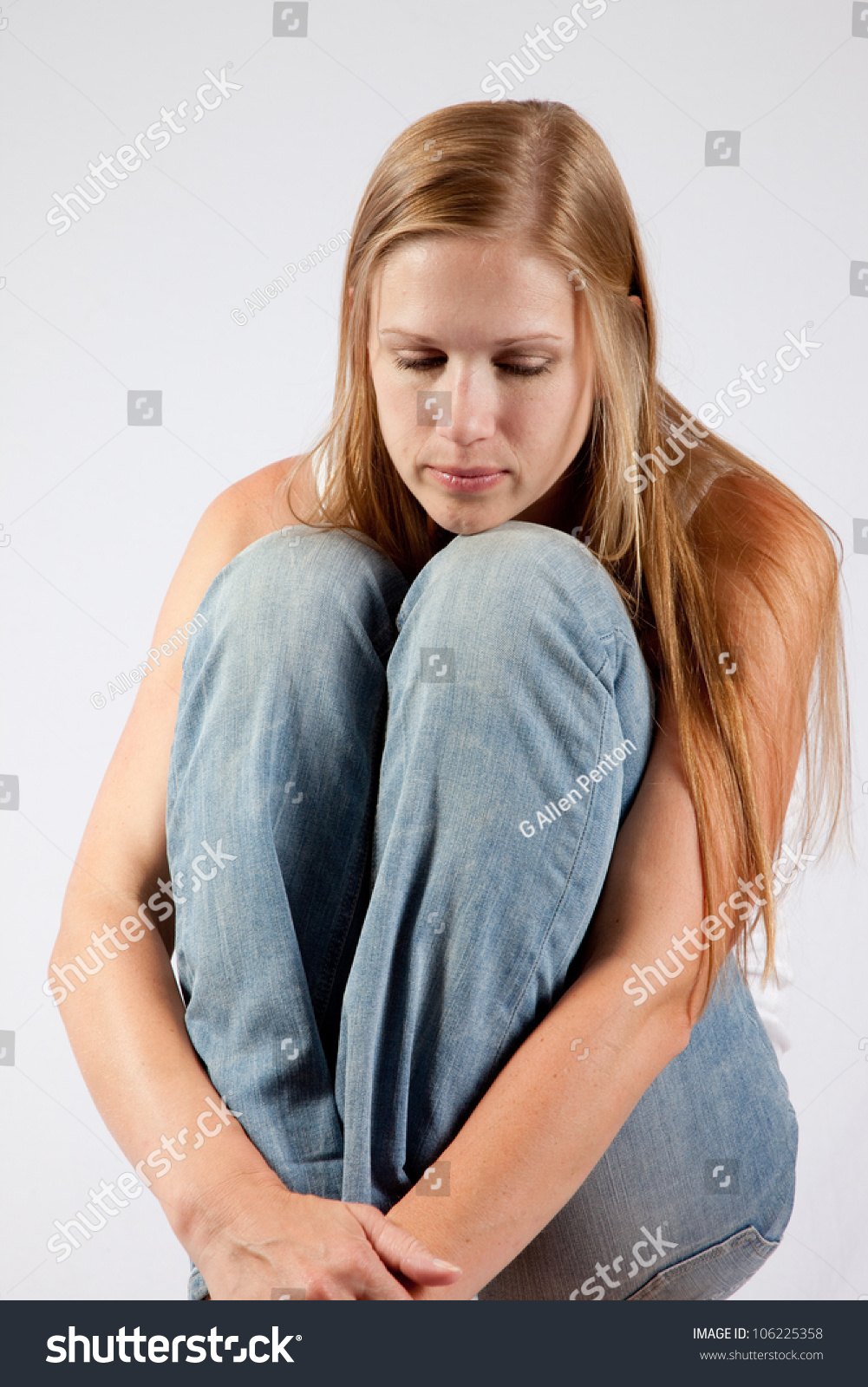 Pretty Blond Woman Sitting And Thinking Sadly With Her Arms Wrapped Around Her Legs And Looking