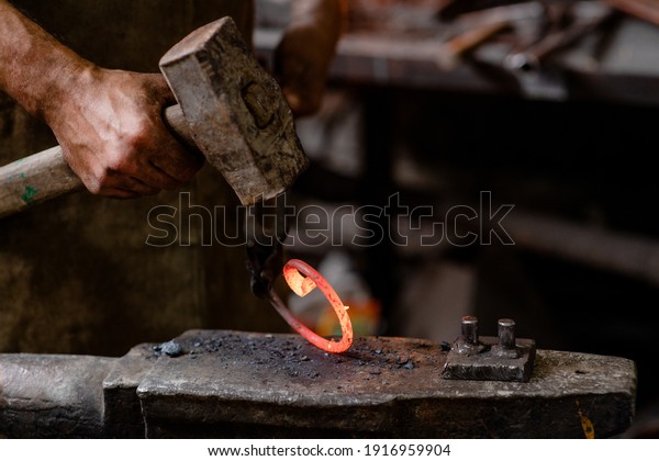 Blacksmith is processing a hot metal object of a spiral shape at anvil ...