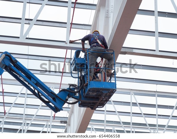 construction worker at construction site using lifting boom machinery