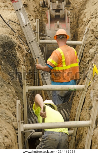 Construction workers using trench shoring equipment to backfill and ...