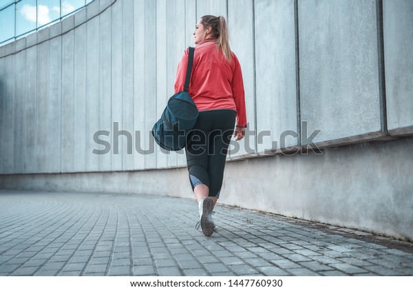 Going home. Back view of plus size woman in sport clothes carrying her ...