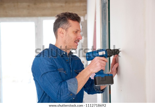 Handyman using cordless drill while working on construction site.