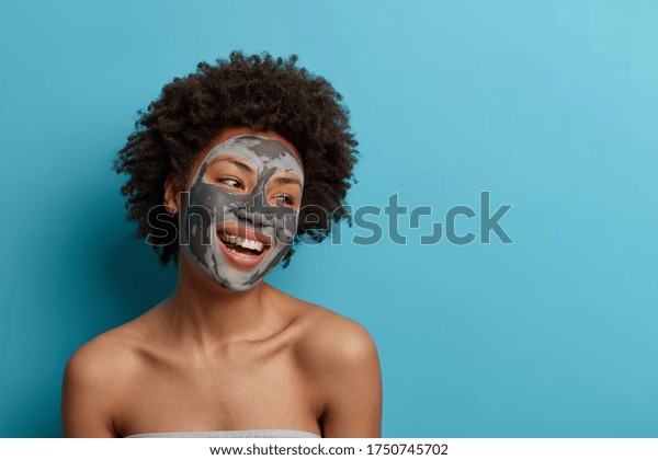 Joyful positive dark skinned curly woman stands naked indoor, applies ... Joyful positive dark skinned curly woman stands naked indoor, applies ...