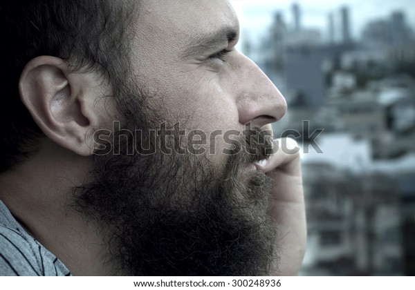 Side view of a guy with a beard on the phone, blurred cityscape in the ...