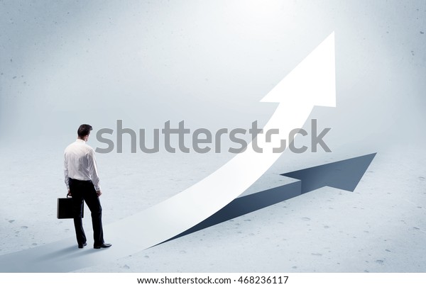 A young adult salesman standing in front of a big arrow pointing up ... A young adult salesman standing in front of a big arrow pointing up ...