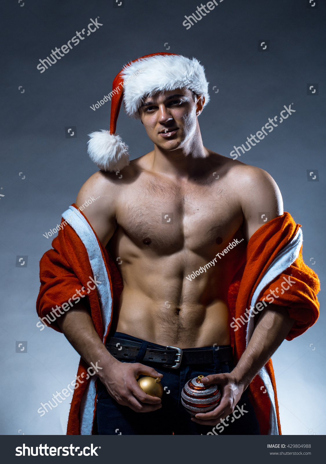 Young Handsome Man With Muscular Body Bare Chest And Torso In Santa Claus Coat And Hat Posing In